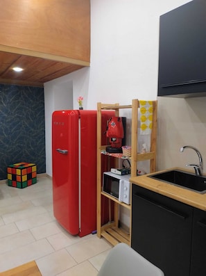 Cozinha compacta com geladeira vermelha, estante de madeira, pia e um cubo mágico no chão.