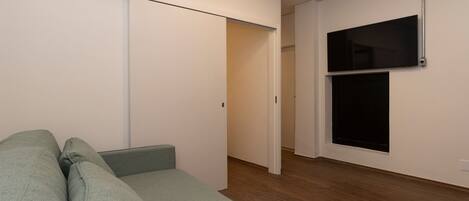 Quarto com porta de correr, televisão de tela plana na parede e sofá cinza.