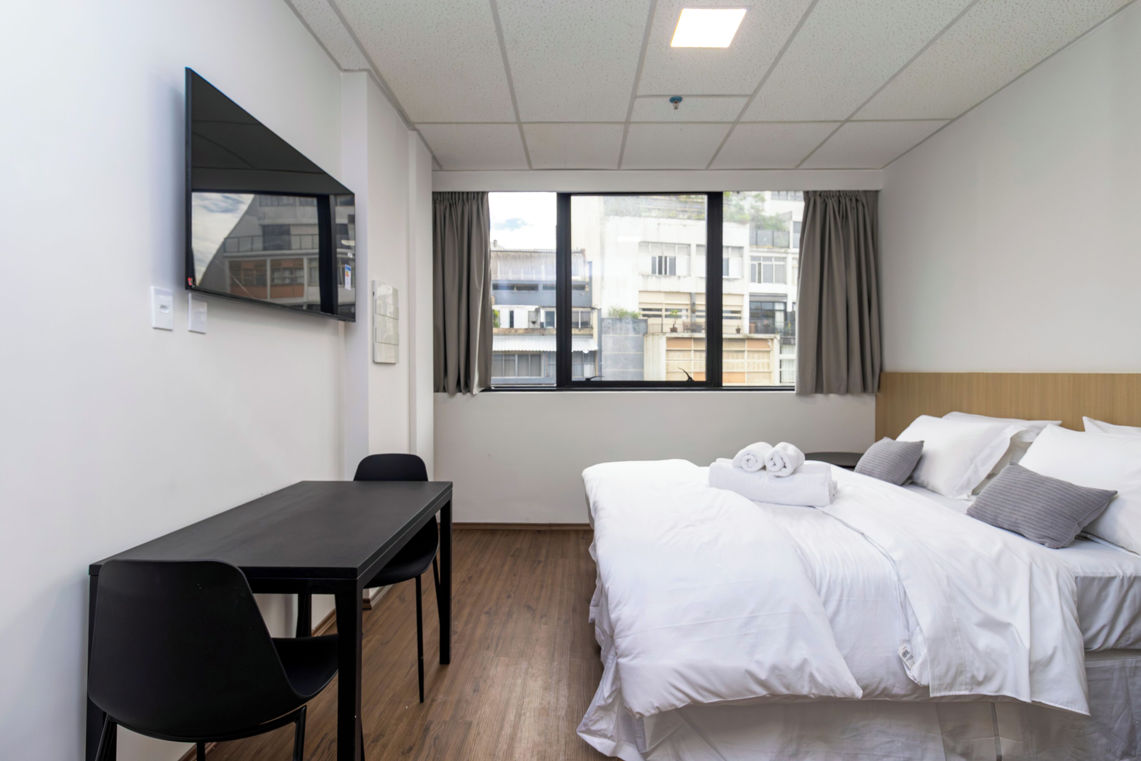 Quarto de hotel com uma cama, uma escrivaninha e uma cadeira.
