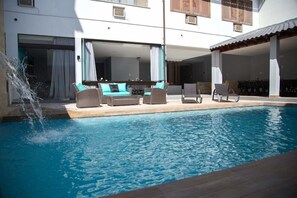 Piscina com um elemento aquático, área de estar externa e um terraço coberto.