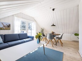 Um quarto moderno e bem iluminado, com teto alto, área de refeições com mesa e cadeiras redondas, um sofá e uma janela grande.