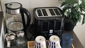 Uma bancada de cozinha com chaleira, torradeira, caneca e um tabuleiro com uma planta.