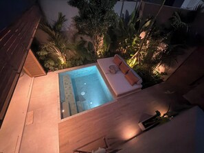 Uma banheira de hidromassagem retangular com borda branca, rodeada por plantas e um deck de madeira.