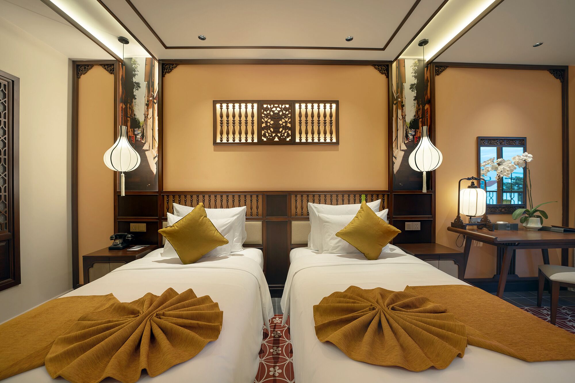Quarto de hotel com duas camas, uma escrivaninha, uma cadeira, um abajur e um objeto decorativo na parede.