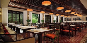 Um restaurante com várias mesas e cadeiras, janelas amplas e lanternas penduradas.