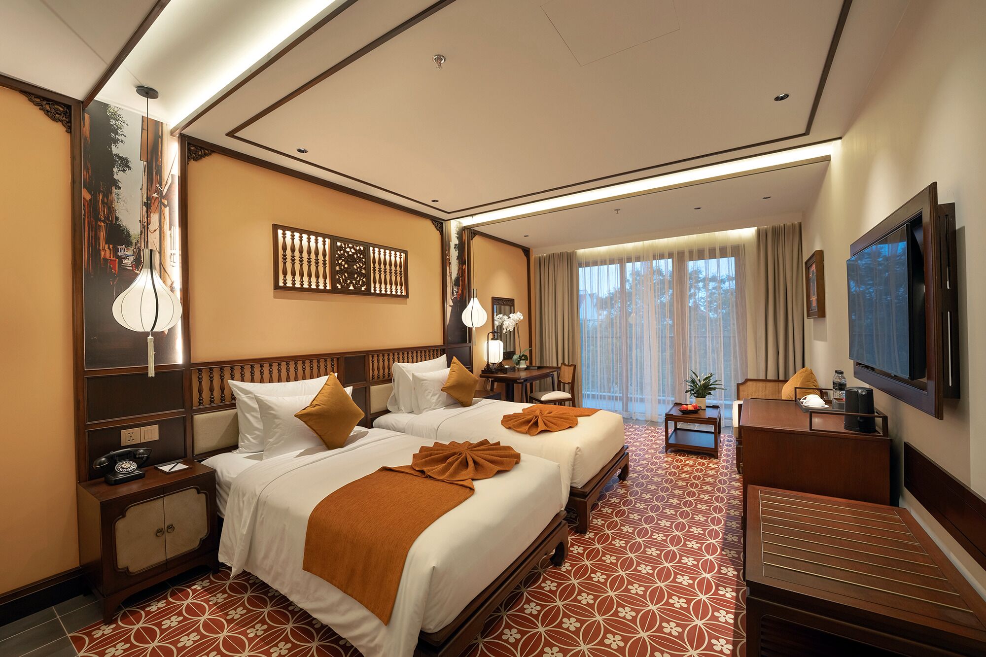 Quarto de hotel com duas camas, uma escrivaninha, uma televisão e uma janela grande com cortinas.