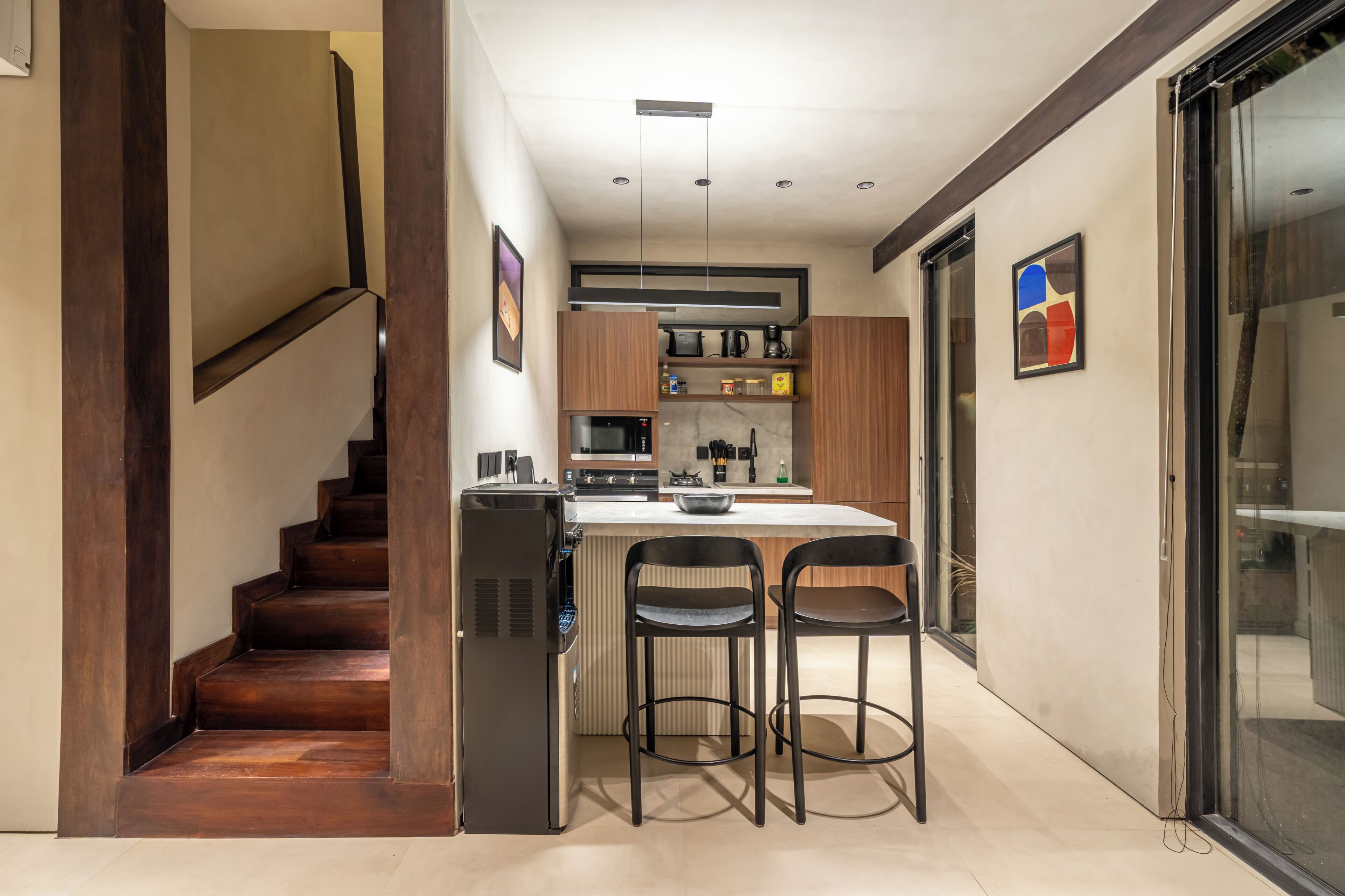 Uma cozinha moderna com ilha central, banquetas e uma escada.