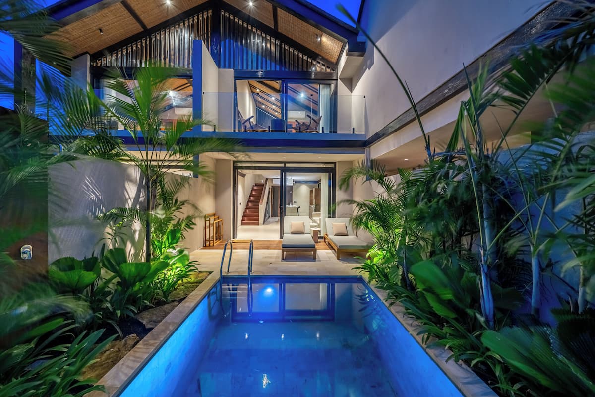 Uma casa moderna de dois andares com piscina, área de estar externa e vegetação exuberante.