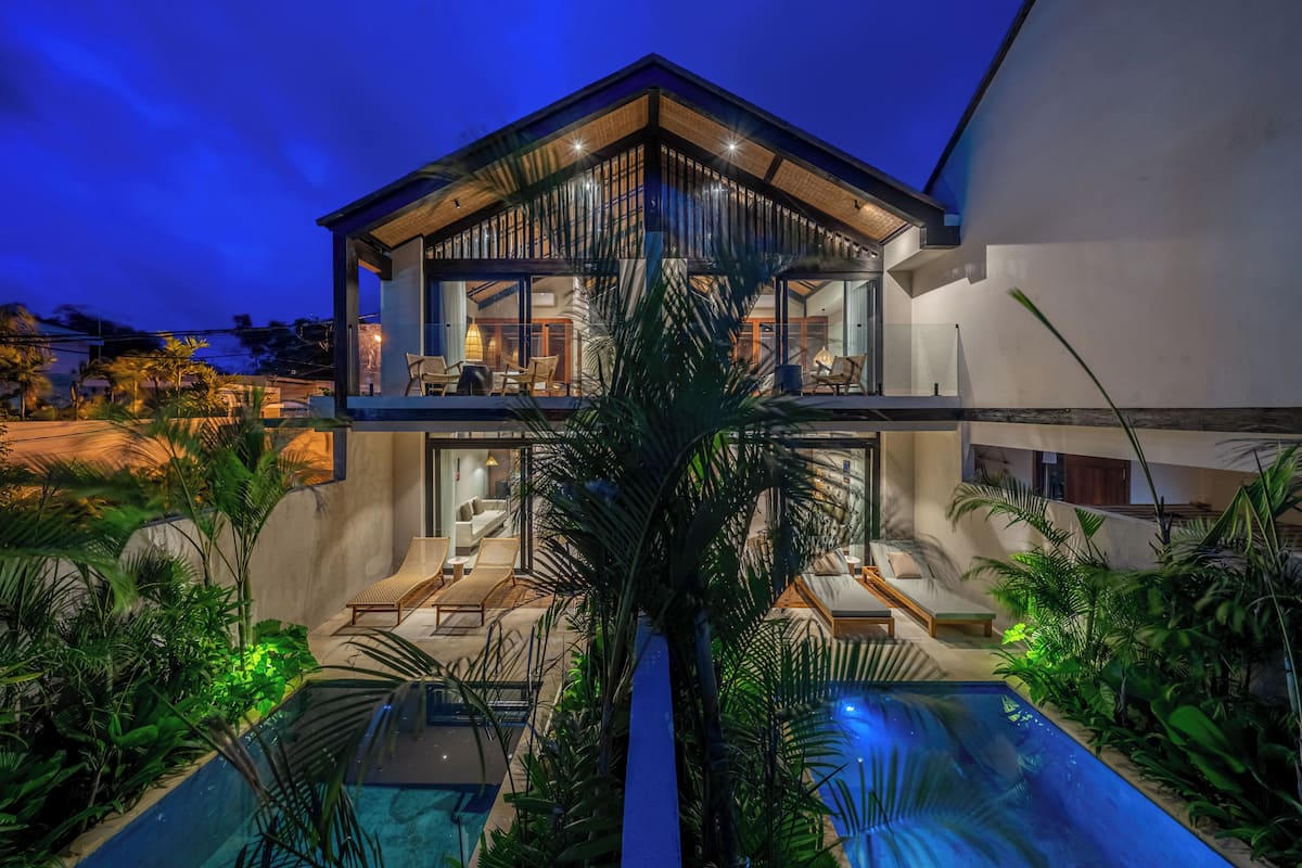 Uma casa moderna de dois andares com piscina, área de estar externa e vegetação exuberante.