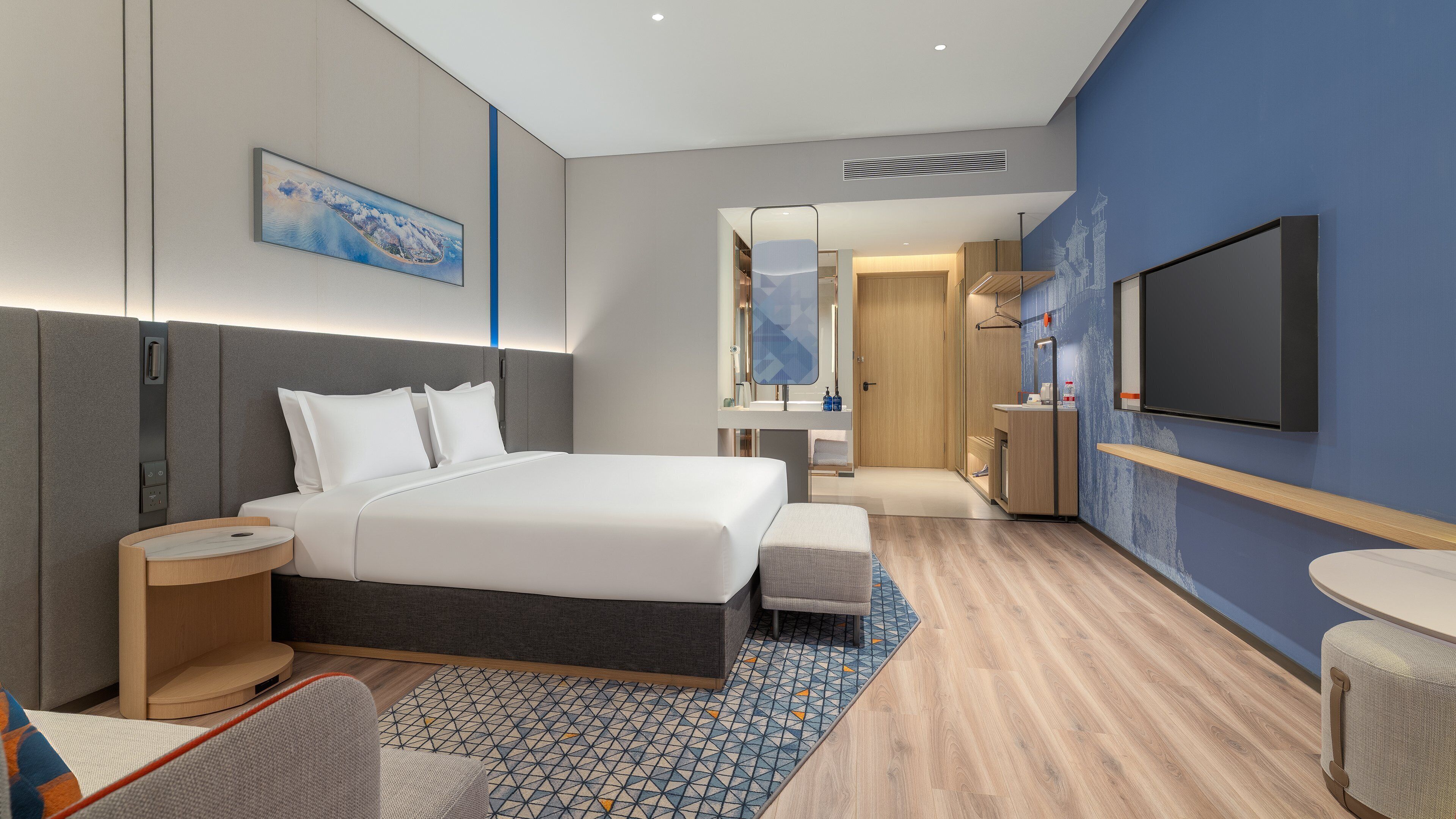 Quarto de hotel moderno com uma cama grande, mesas de cabeceira, televisão e banheiro com espelho e pia.