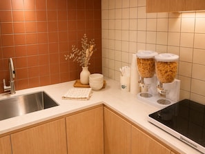 Uma cozinha com pia de aço inoxidável, armários de madeira, bancada branca, fogão branco e dois dispensadores de cereal.
