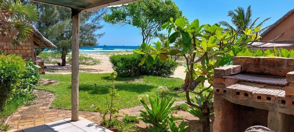 Um pátio com churrasqueira, vista para a praia e um caminho que leva a um edifício.