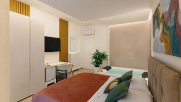 Quarto de hotel com cama, escrivaninha, cadeira, mesinha, planta e um quadro na parede.