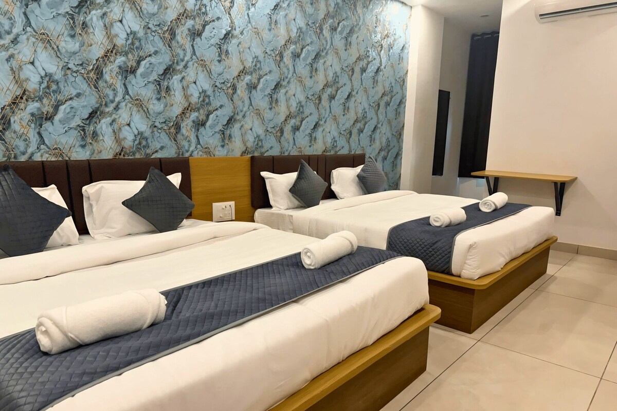 Quarto de hotel com duas camas, parede com padrão marmorizado, cabeceira de madeira e uma mesinha.