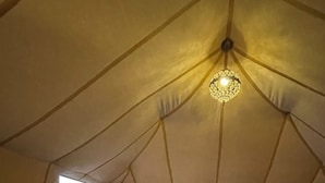 Quarto tipo tenda com uma cama, um banco com toalhas, um tapete e um candeeiro suspenso.