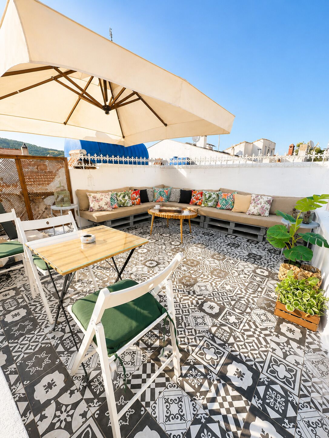 Uma área externa com assentos, um piso estampado, uma mesa de madeira e um grande guarda-sol.
