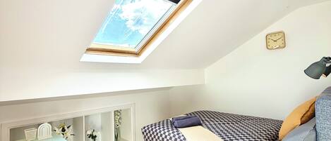 Quarto compacto com cama, escrivaninha e claraboia.