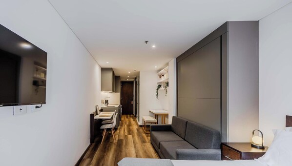 Quarto de hotel moderno com sofá, uma pequena mesa, abajur e vista para o corredor.