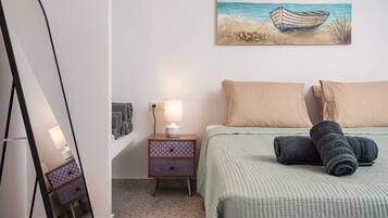 Quarto com cama, travesseiros, mesa de cabeceira com abajur, quadro de um barco na parede e espelho.