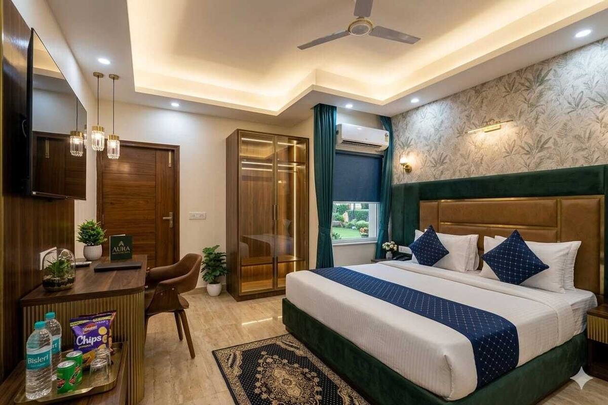 Quarto de hotel com cama, escrivaninha com cadeira, televisão, guarda-roupa e ventoinha no teto.