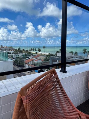 Quarto com vista para a praia e para a cidade, uma cadeira de vime e paredes azulejadas.