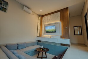 Uma sala de estar moderna com sofá seccional, mesa redonda pequena, TV montada e um armário embutido com detalhe em parede de mármore.