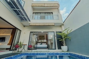 Um edifício moderno de dois andares com varanda, porta de entrada de vidro, piscina pequena e um vaso de planta.