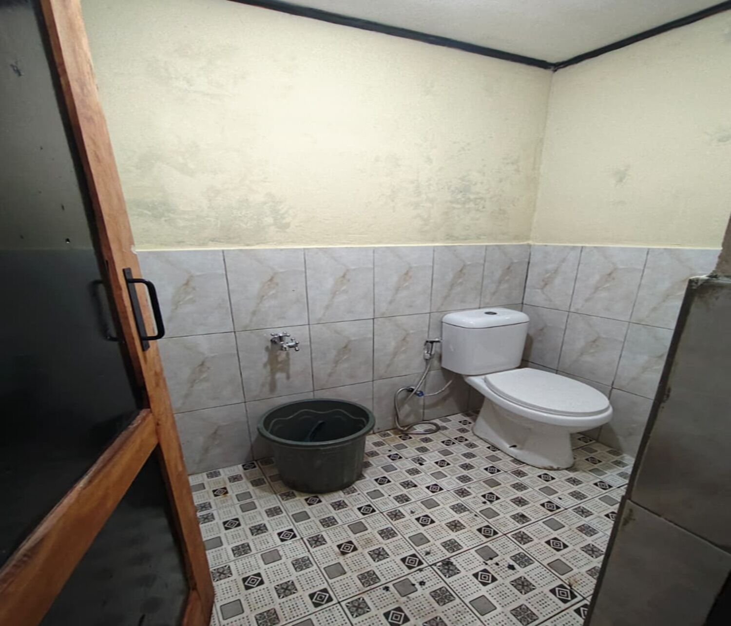Um banheiro pequeno com vaso sanitário, um balde e paredes azulejadas.