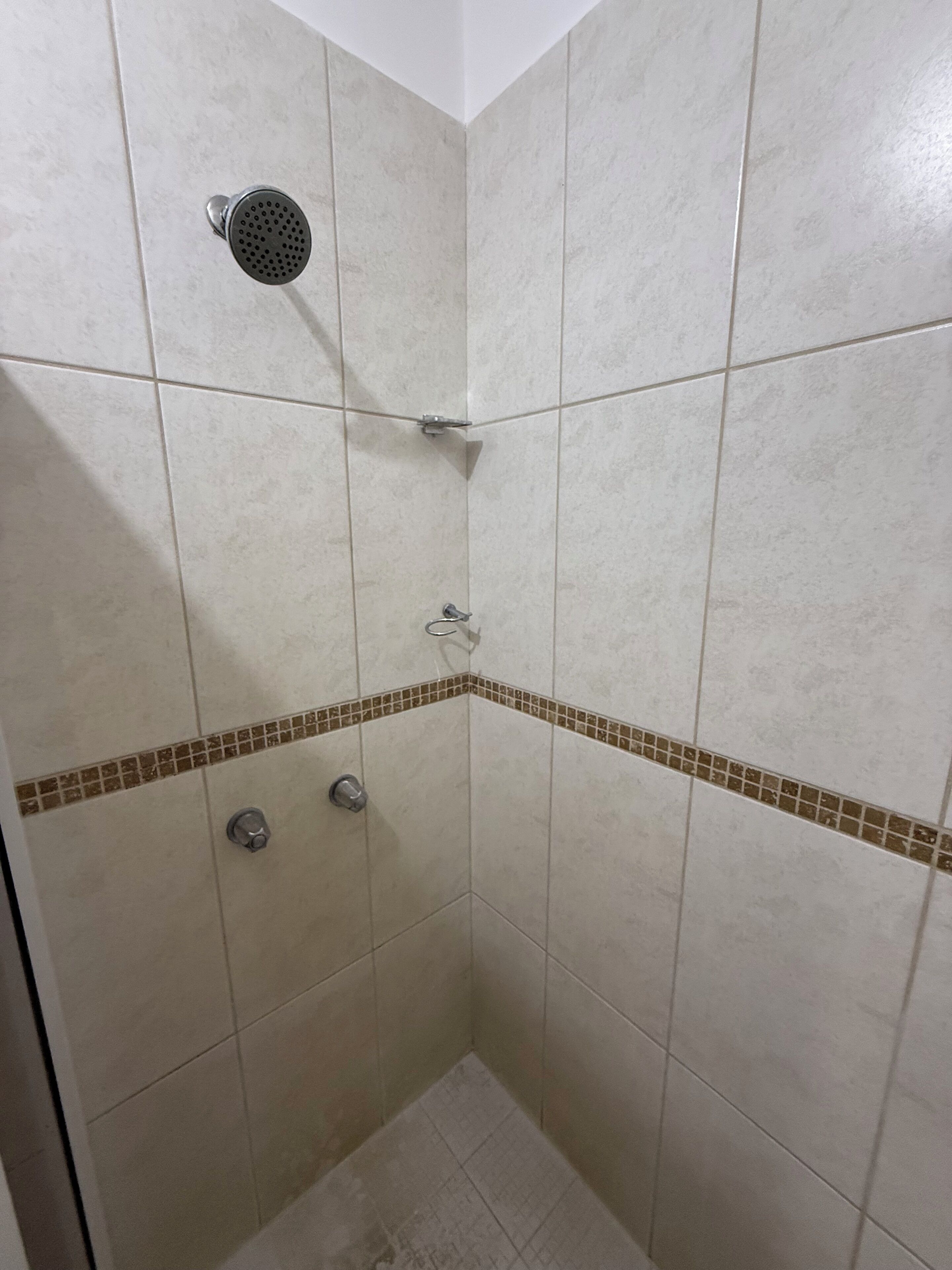 Chuveiro com chuveiro manual, comando fixado na parede e piso revestido de azulejos.