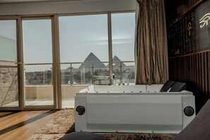Quarto moderno com uma janela grande, um sofá branco e vista para pirâmides.