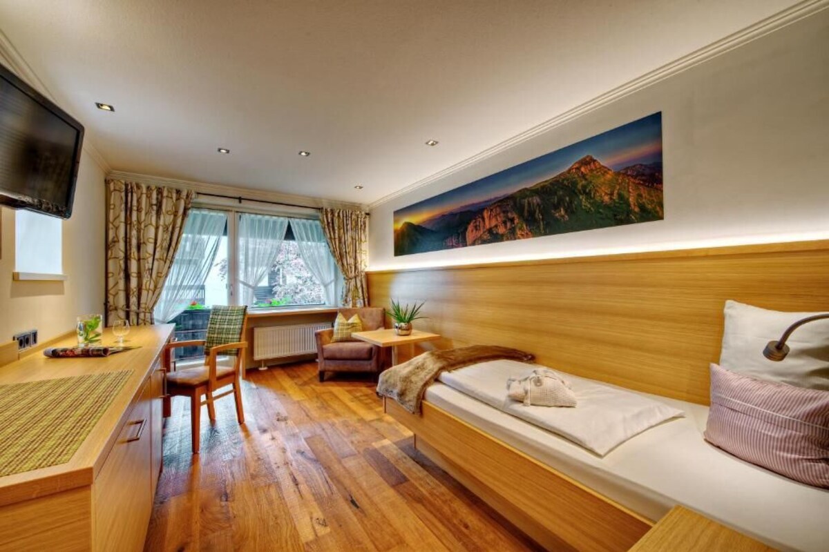 Quarto com cama de madeira, escrivaninha, cadeira, televisão e uma grande pintura na parede.