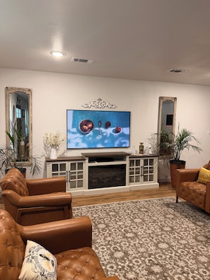 Sala de estar com sofás de couro, lareira, televisão e espelhos decorativos.