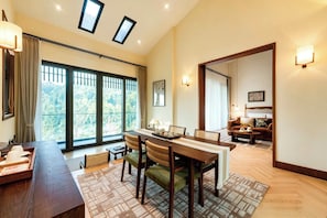 Um quarto amplo com uma mesa de jantar, cadeiras, um sofá e uma janela grande com vista para árvores.