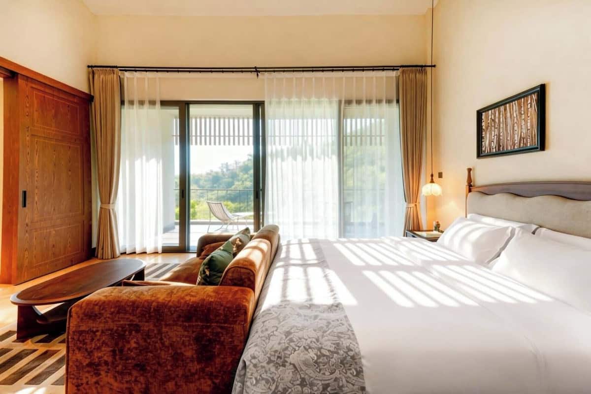 Quarto de hotel com cama, sofá, escrivaninha e vista para o exterior.