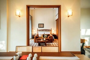 Quarto de hotel com uma cama, um espaço de estar com uma mesa e cadeiras, e duas luminárias fixadas na parede.