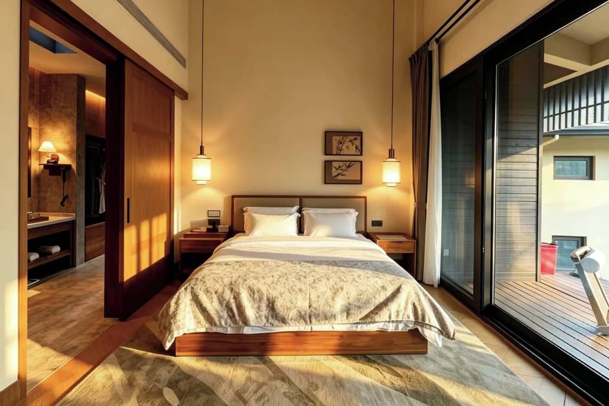Quarto moderno com uma cama grande, abajures, cabeceira de madeira e vista por uma janela ampla.