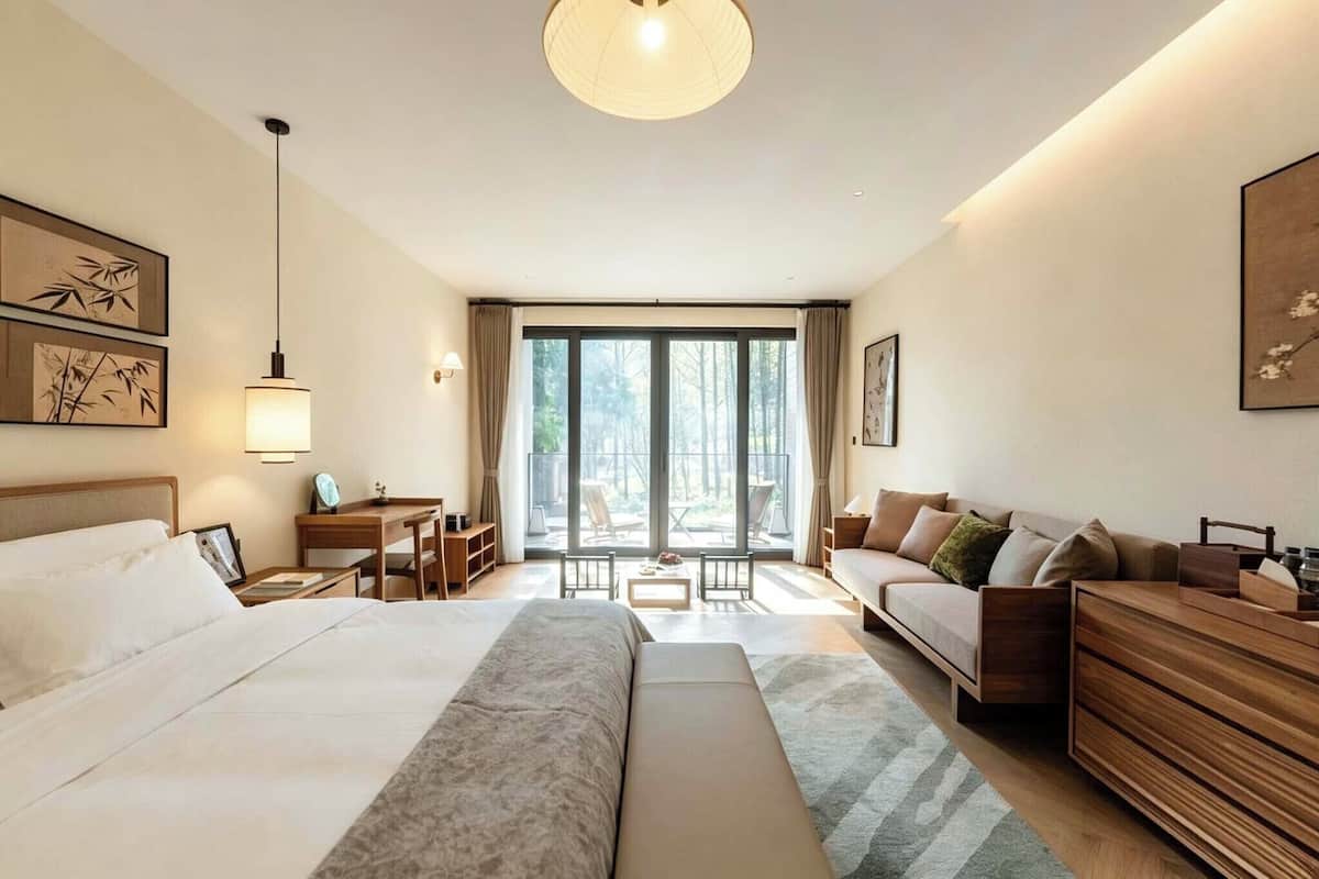 Quarto de hotel com uma cama grande, um sofá, uma escrivaninha e vista para o exterior.