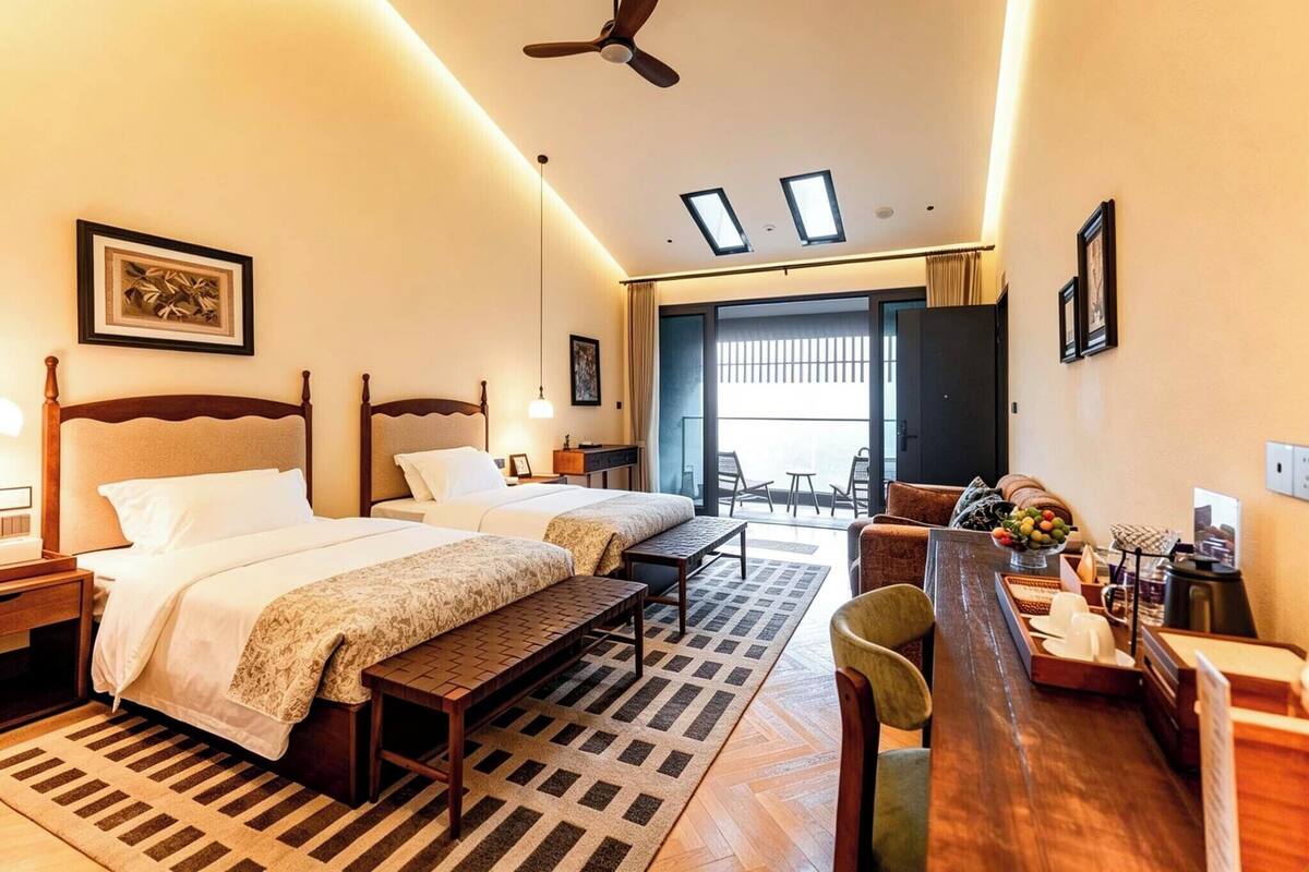 Quarto de hotel com duas camas, uma escrivaninha, uma cadeira, um ventilador de teto e vista para o exterior.