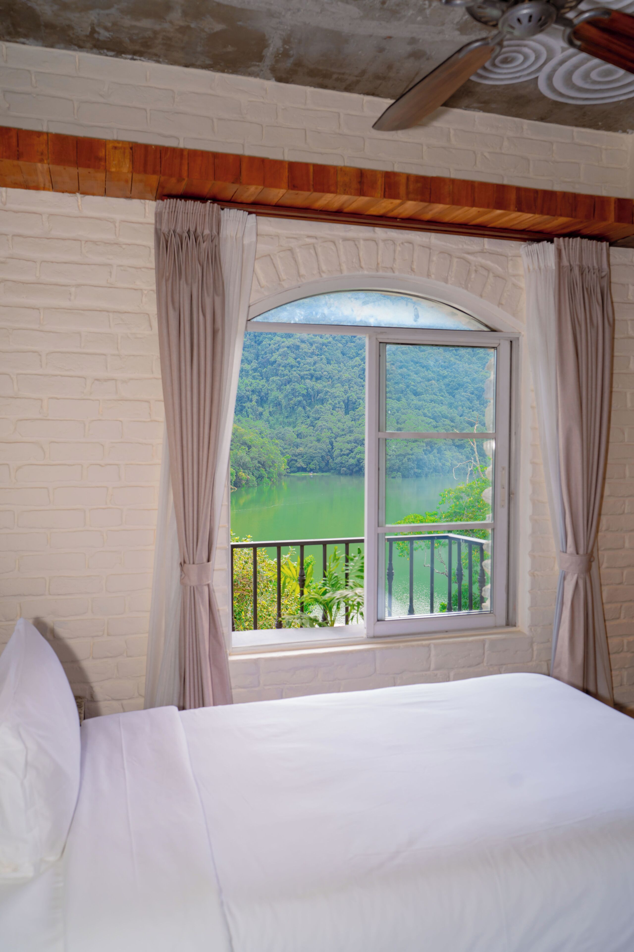 Quarto com cama, janela com cortinas e vista para um lago.