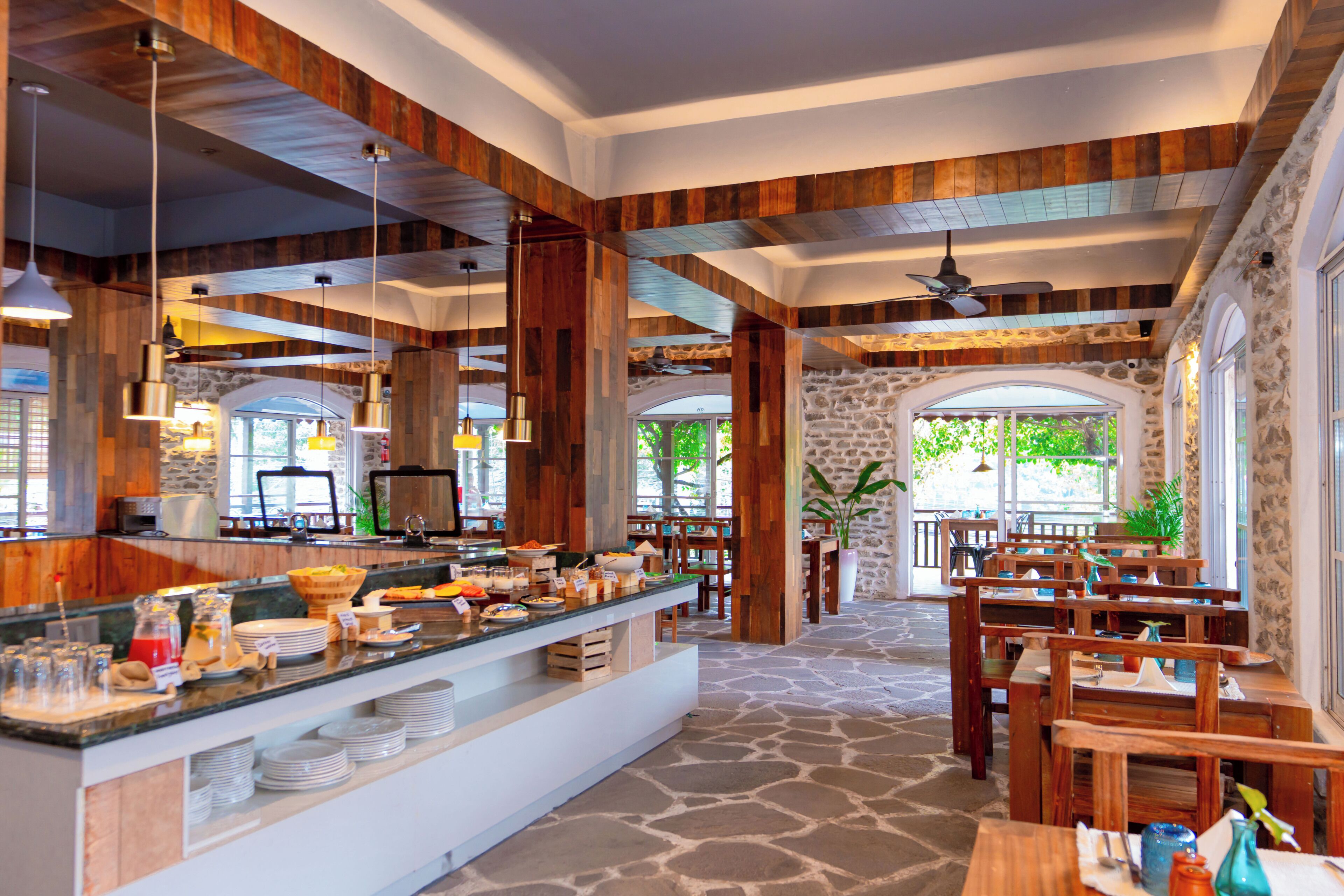Restaurante com piso de pedra, vigas de madeira e área de buffet com diversos pratos.