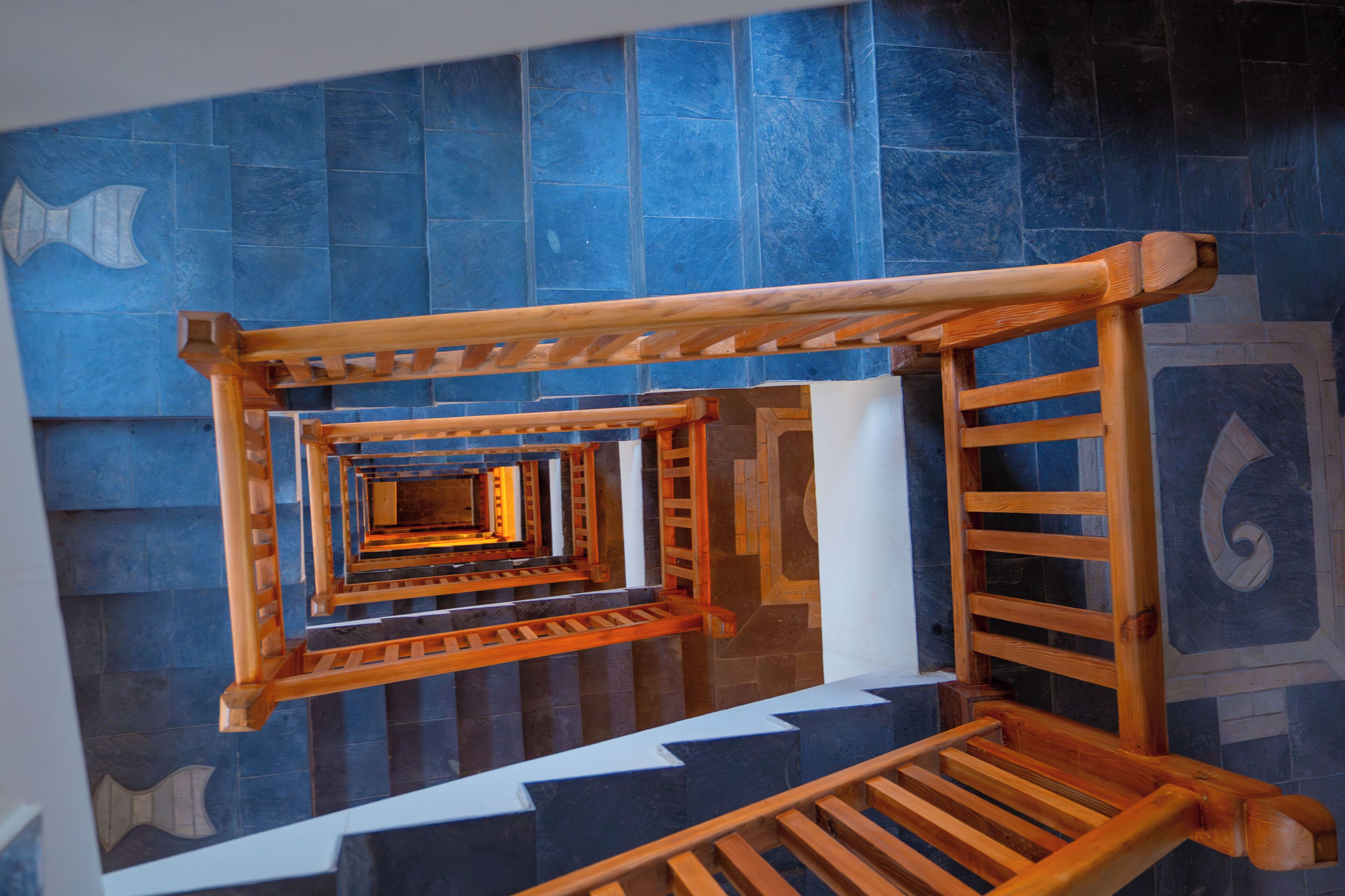 Escadaria em espiral com corrimãos de madeira e parede revestida de azulejos azuis.