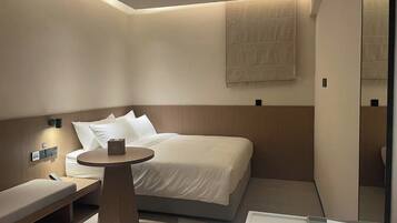Quarto de hotel moderno com cama, mesa de cabeceira e uma pequena mesa redonda.