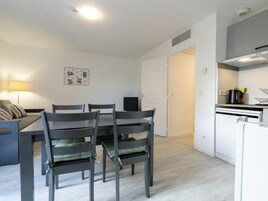 Uma cozinha moderna com eletrodomésticos brancos, um espaço de jantar com mesa e cadeiras, e uma porta que dá para outro cômodo.