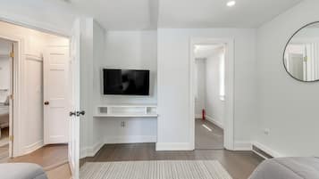 Quarto moderno com televisão de tela plana na parede, um espelho grande e uma porta que dá para outro cômodo.