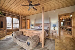 Quarto estilo cabana de madeira com cama de madeira, um banquinho tecido e um ventilador de teto.