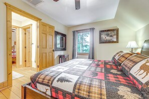 Quarto com uma cama grande, janela com cortinas, mesa de cabeceira e porta que dá para outro cômodo.