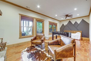 Quarto com piso de madeira, poltronas de couro, mesa de pebolim, cama e janelas amplas.