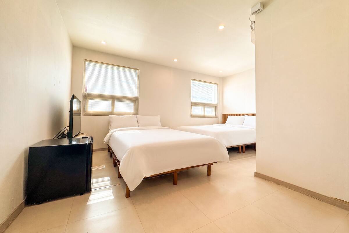 Quarto de hotel com duas camas, uma televisão e uma escrivaninha.
