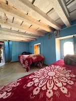 Quarto com uma cama, uma mesa com toalha vermelha, parede azul e teto de madeira.