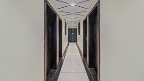 Um corredor comprido e estreito com piso de azulejos, paredes escuras e teto com iluminação embutida.